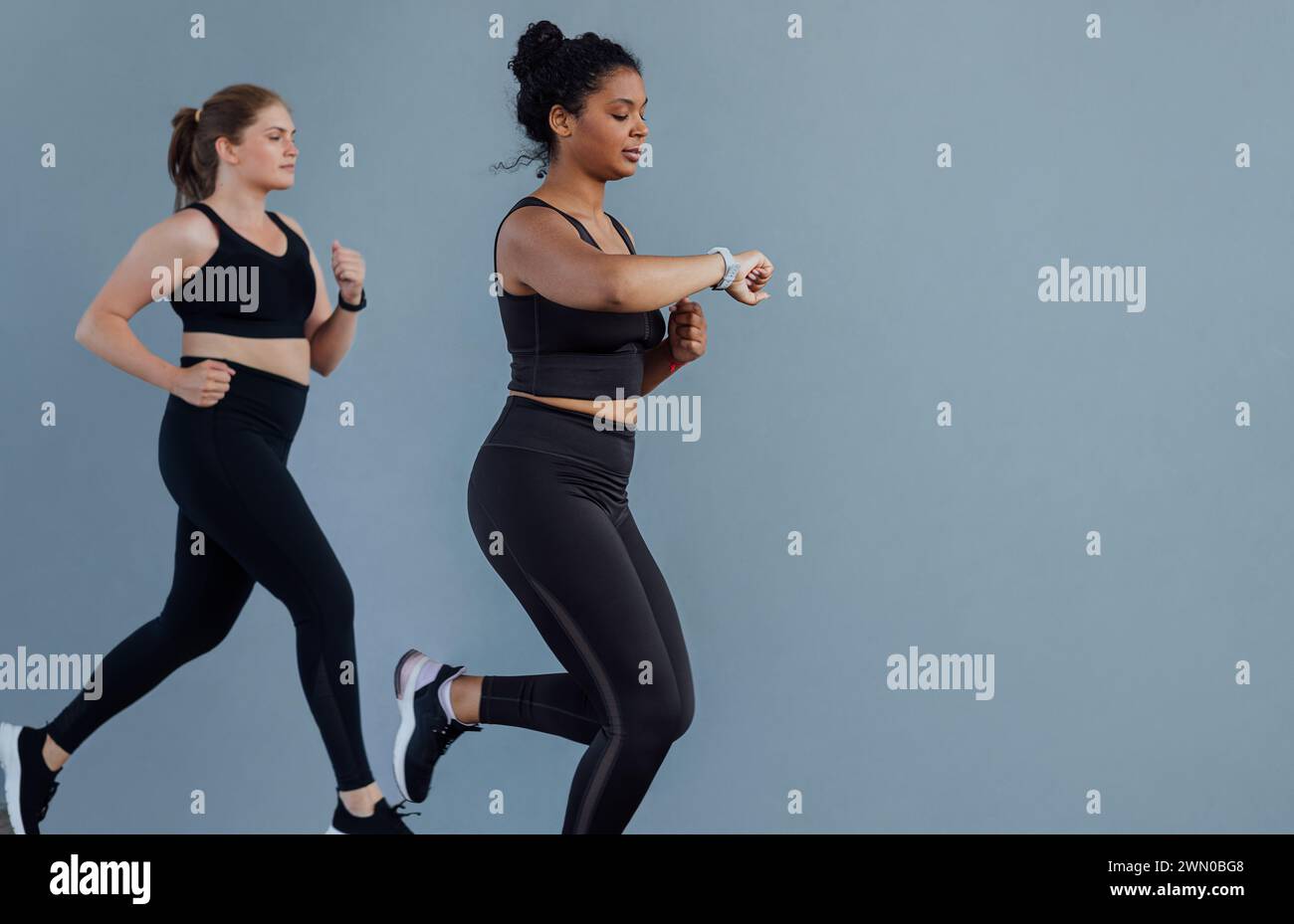 Two females with different body types running outdoors a grey wall ...