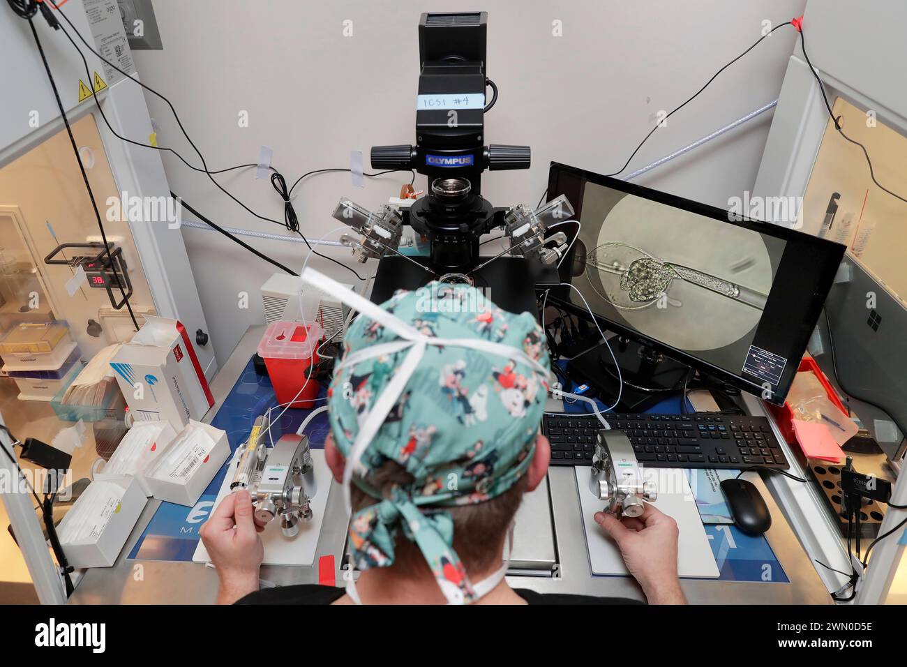 Lab staff use a microscope stand and articulated hand controls to ...