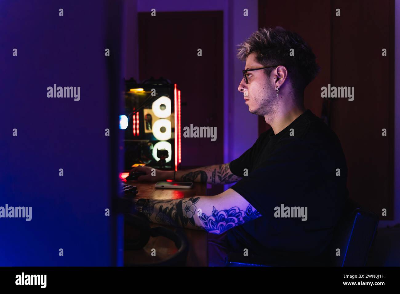 Young man with glasses and tattooed playing video games sitting in his ...