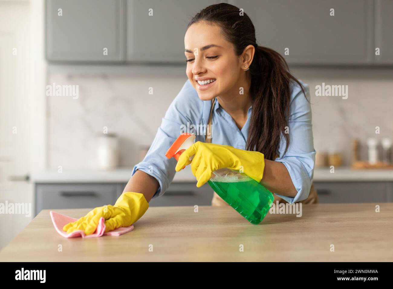 Smiling woman cleaning kitchen counter with spray Stock Photo - Alamy