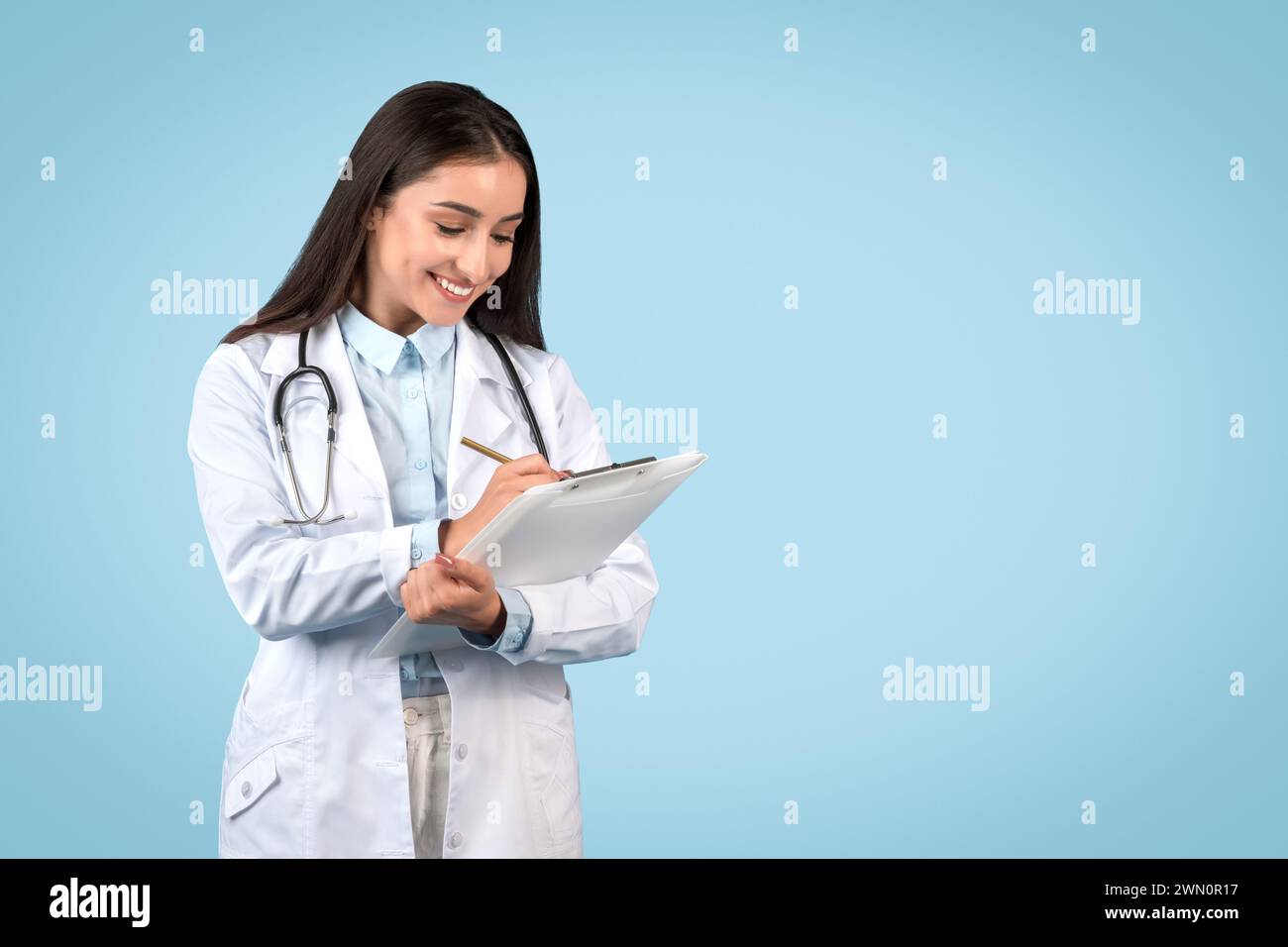 Doctor writing notes on clipboard on light blue backdrop, free space ...