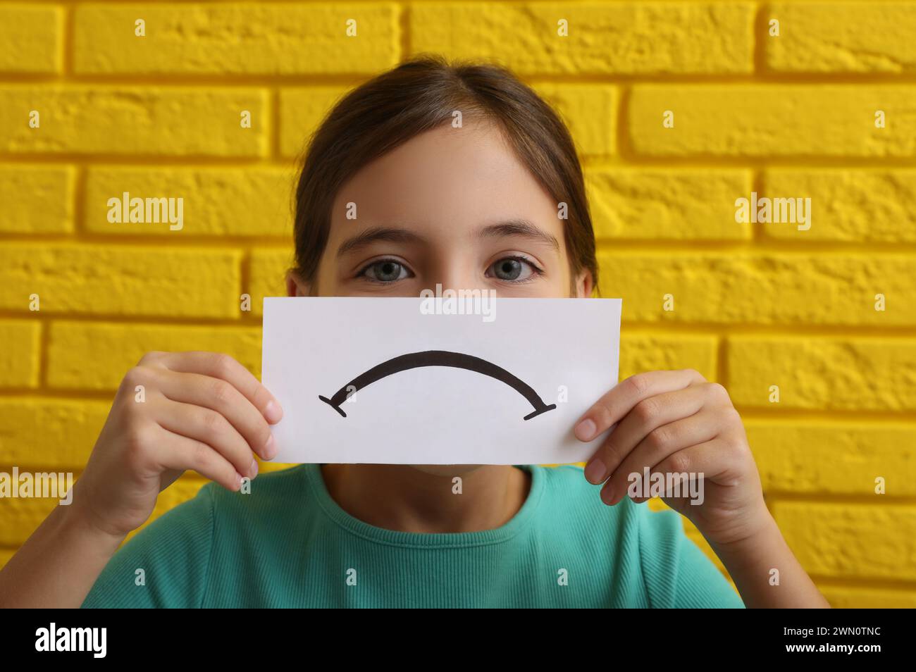 Sad face. Little girl showing feelings with card against yellow brick ...