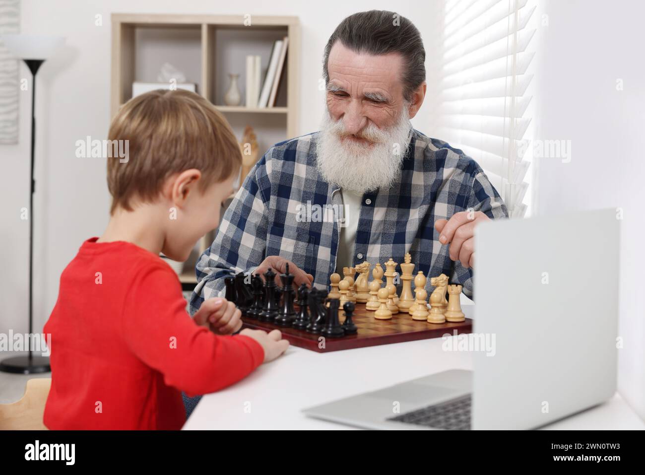 Grandfather and grandson playing chess following online lesson in room ...