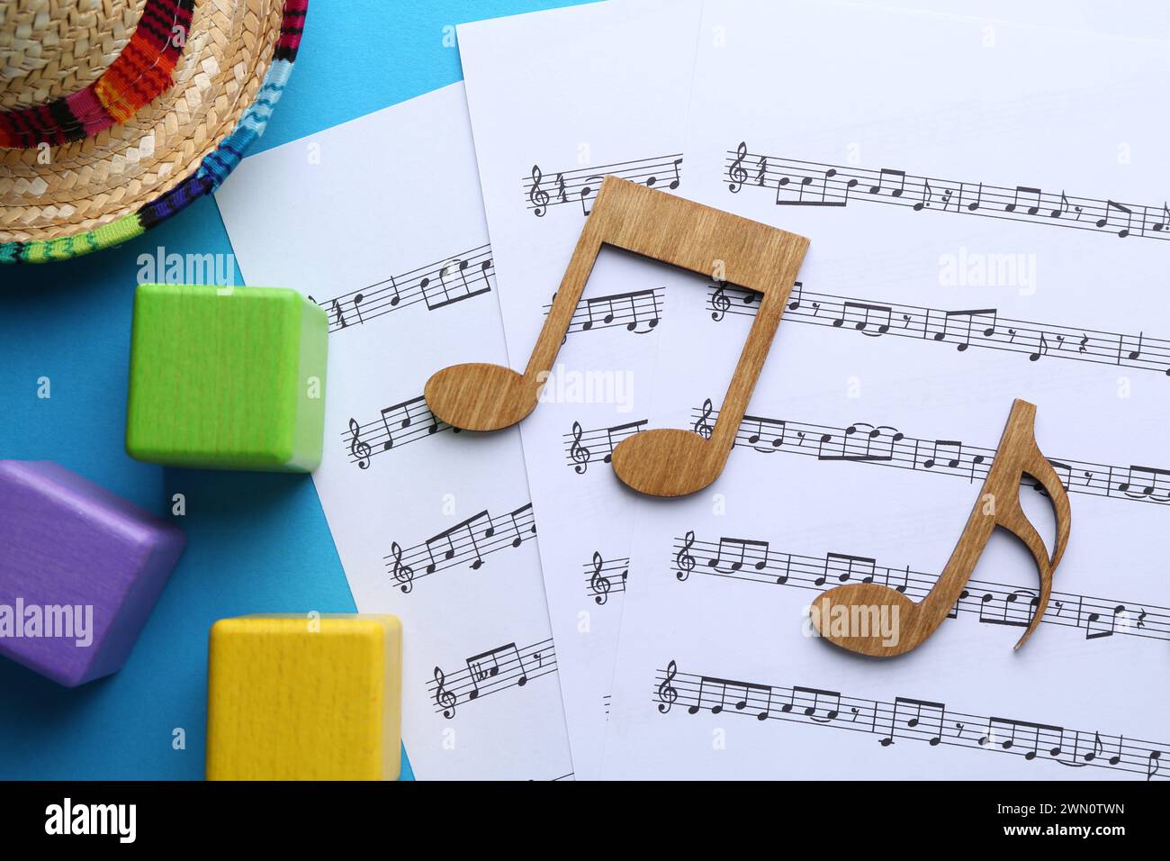 Baby songs. Music sheets, wooden notes, cubes and hat on light blue ...