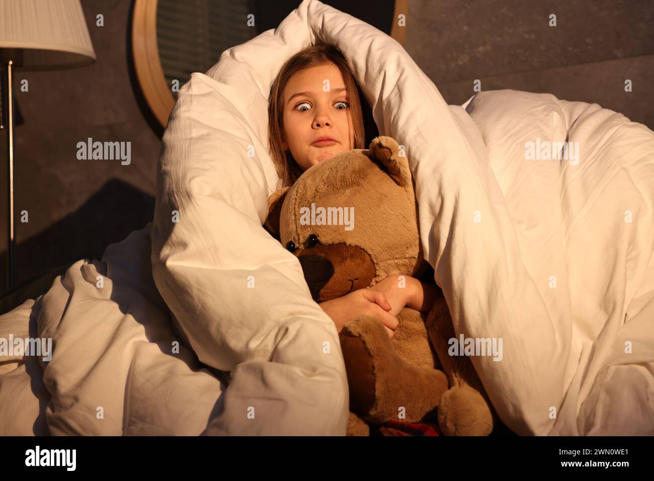 Scared little girl with toy hiding from monster in duvet at night Stock ...