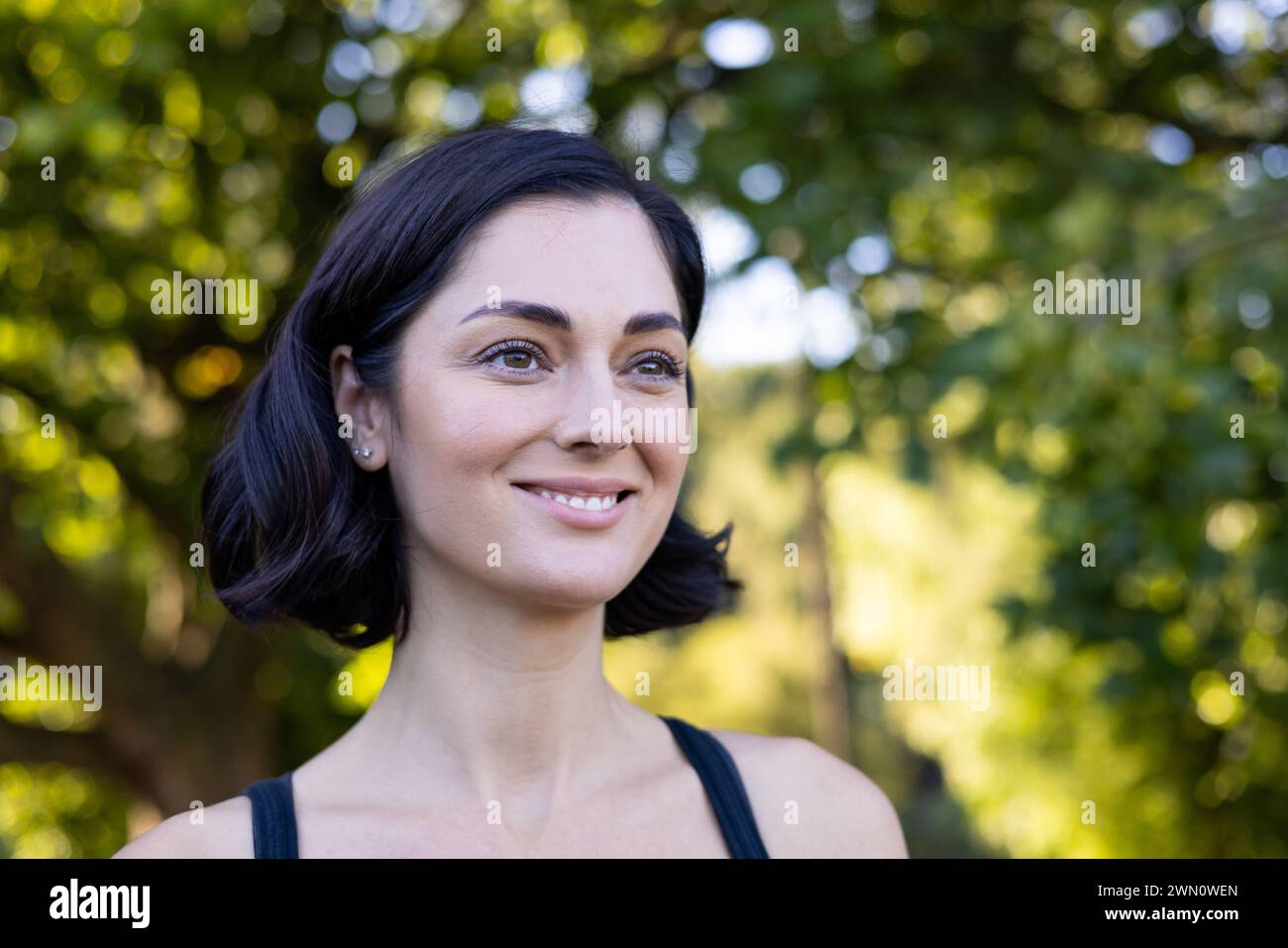 An attractive woman with a subtle smile stands outdoors, her joy ...