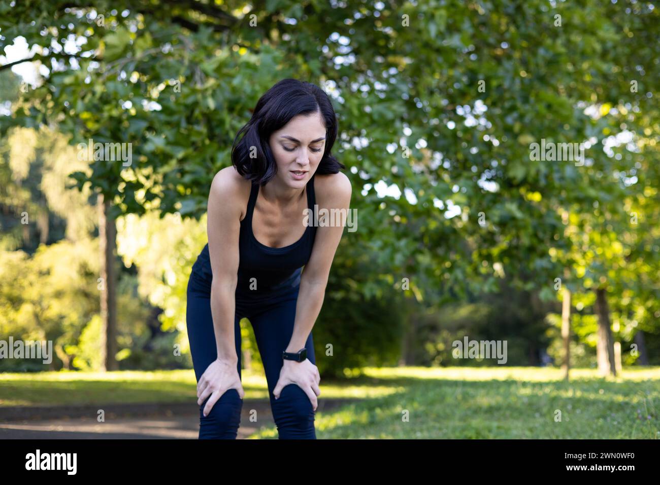 Tired young woman standing bent over in park, resting and shivering ...
