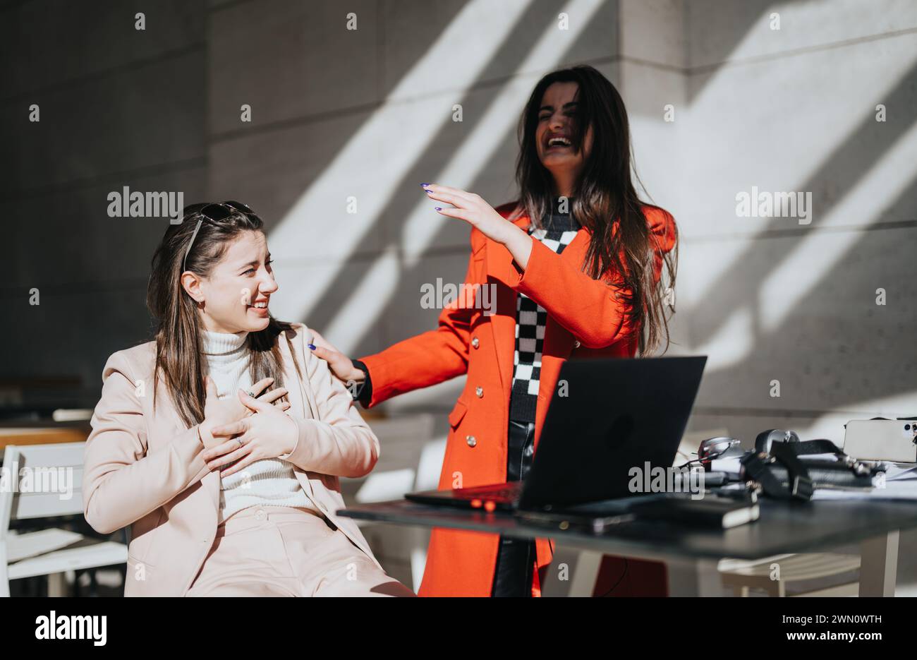 Cheerful female colleagues sharing a light-hearted moment at a sunny ...