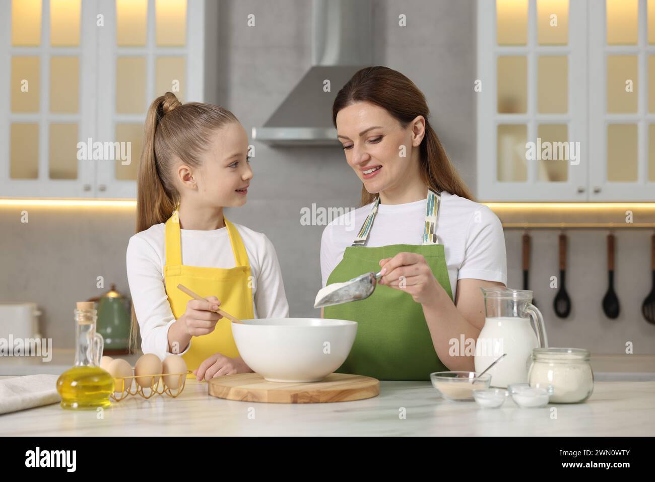 Making bread. Mother and her daughter preparing dough at white table in ...