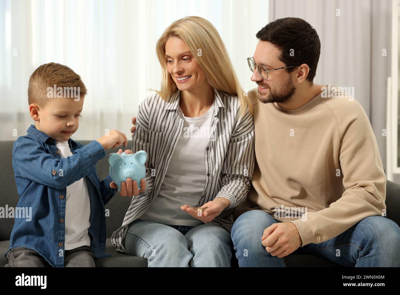 Family budget. Little boy putting coin into piggy bank and his parents ...