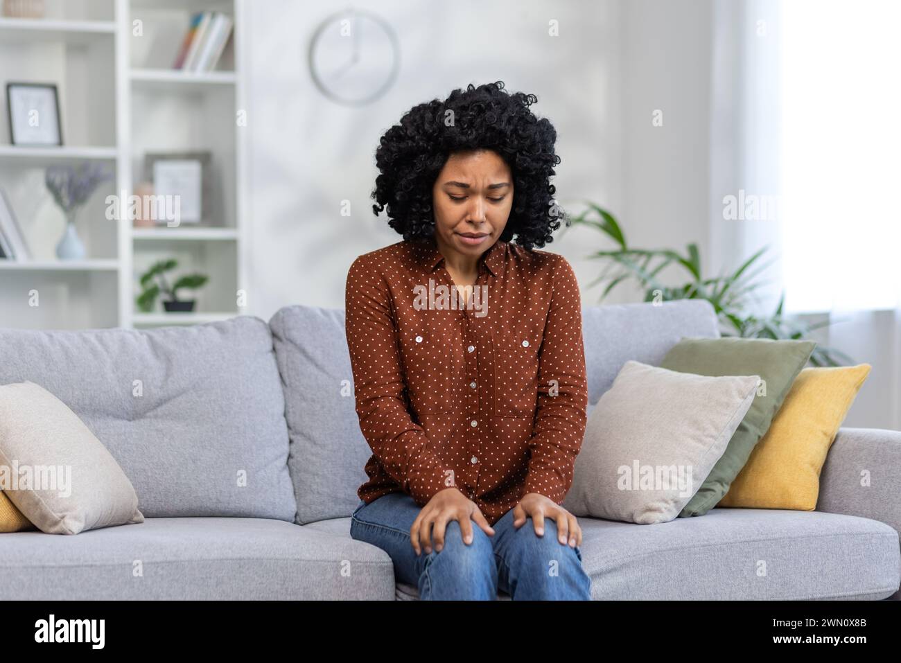 Scared and upset young woman sitting sad on sofa at home, suffering ...