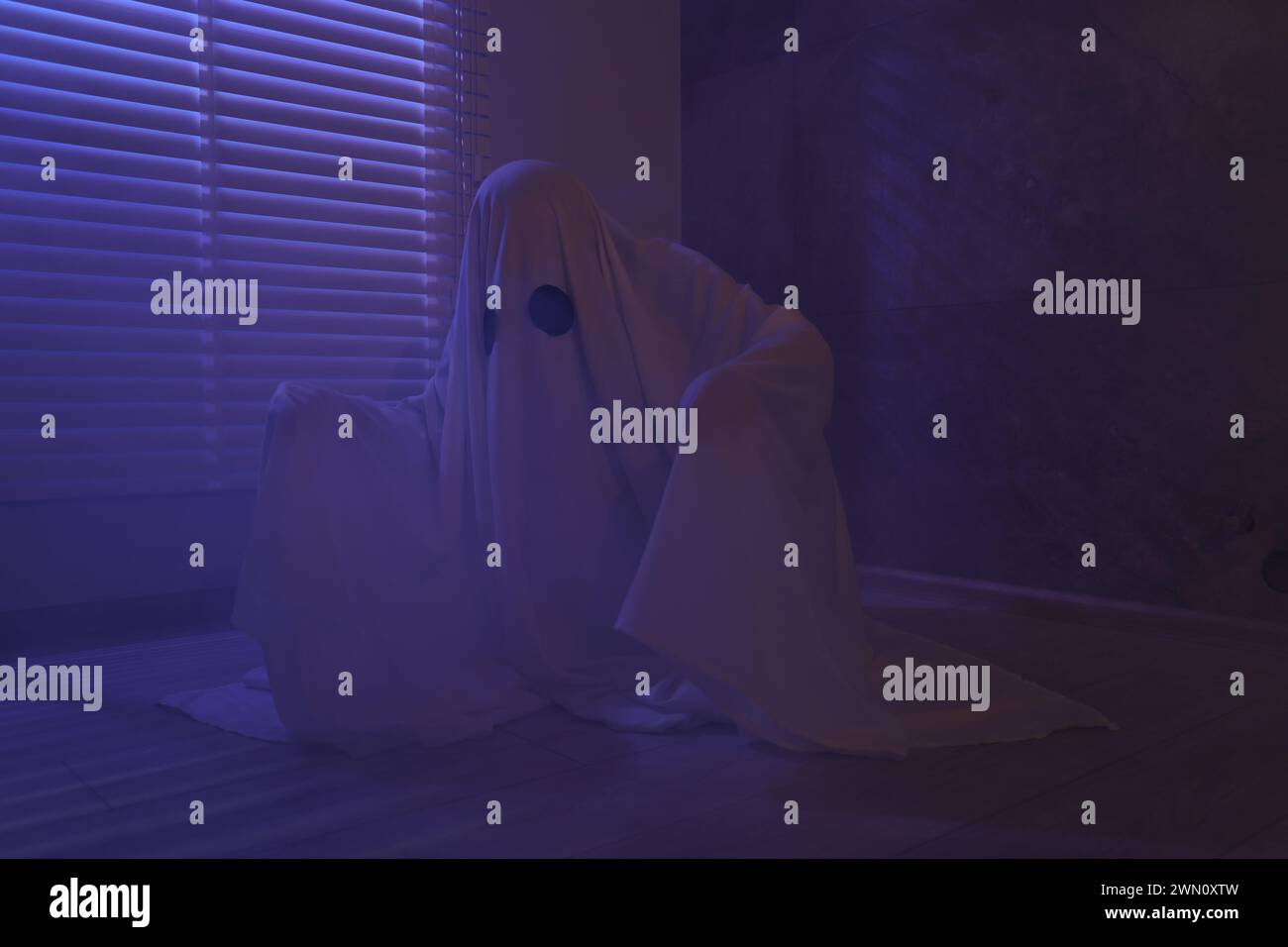 Creepy ghost. Woman covered with sheet near window in color lights ...