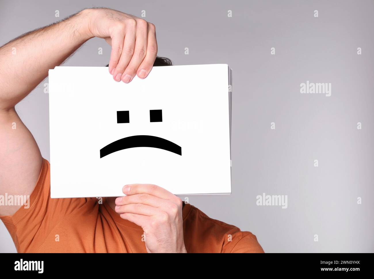 Man hiding behind sheet of paper with sad face on grey background Stock ...