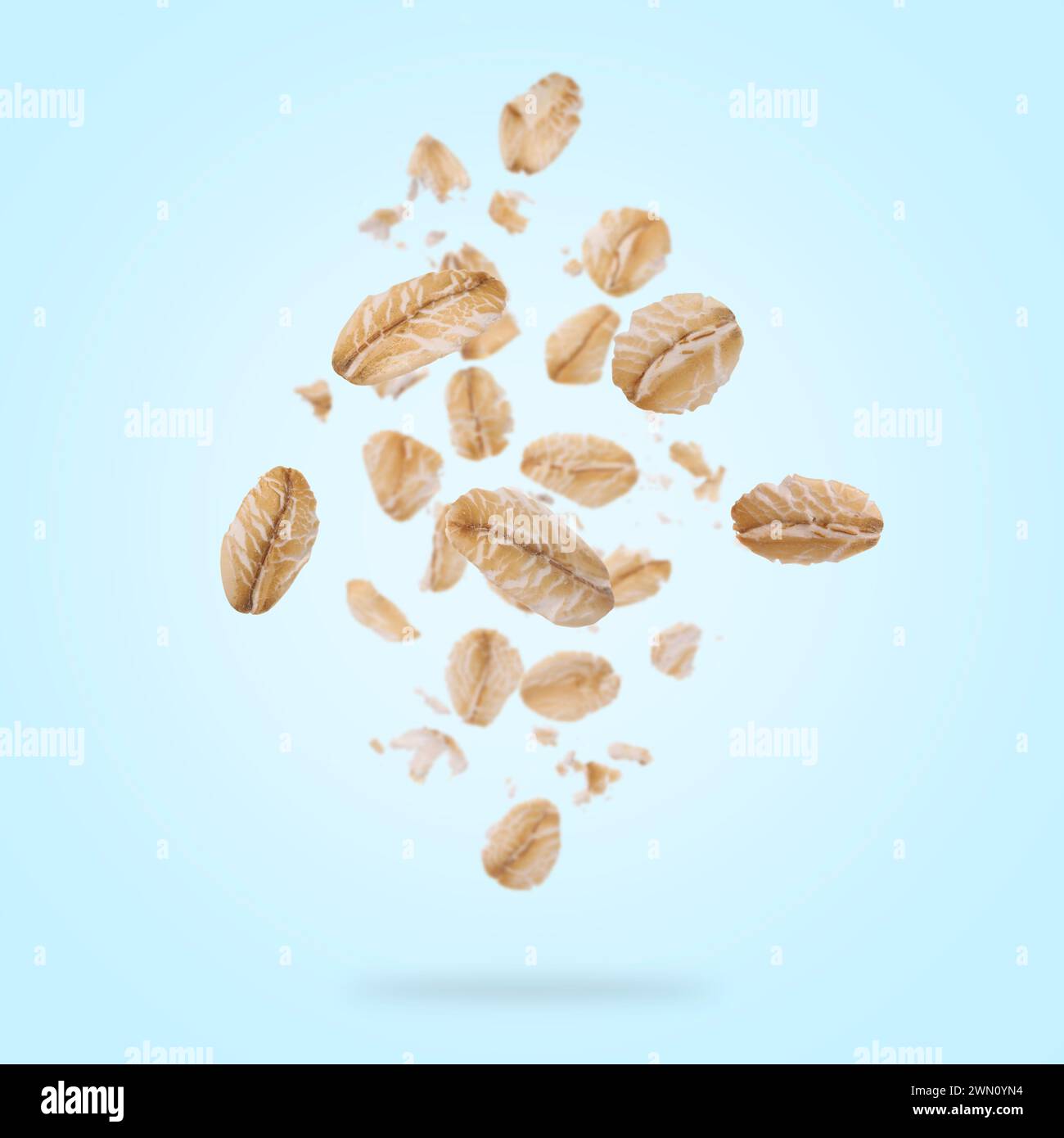 Rolled oat flakes falling on light blue background Stock Photo - Alamy