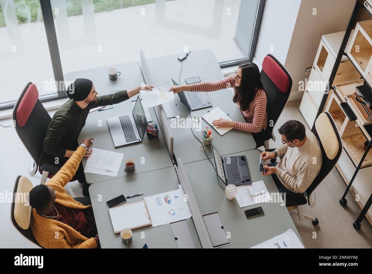 Diverse team collaborating in modern office with laptops and documents ...