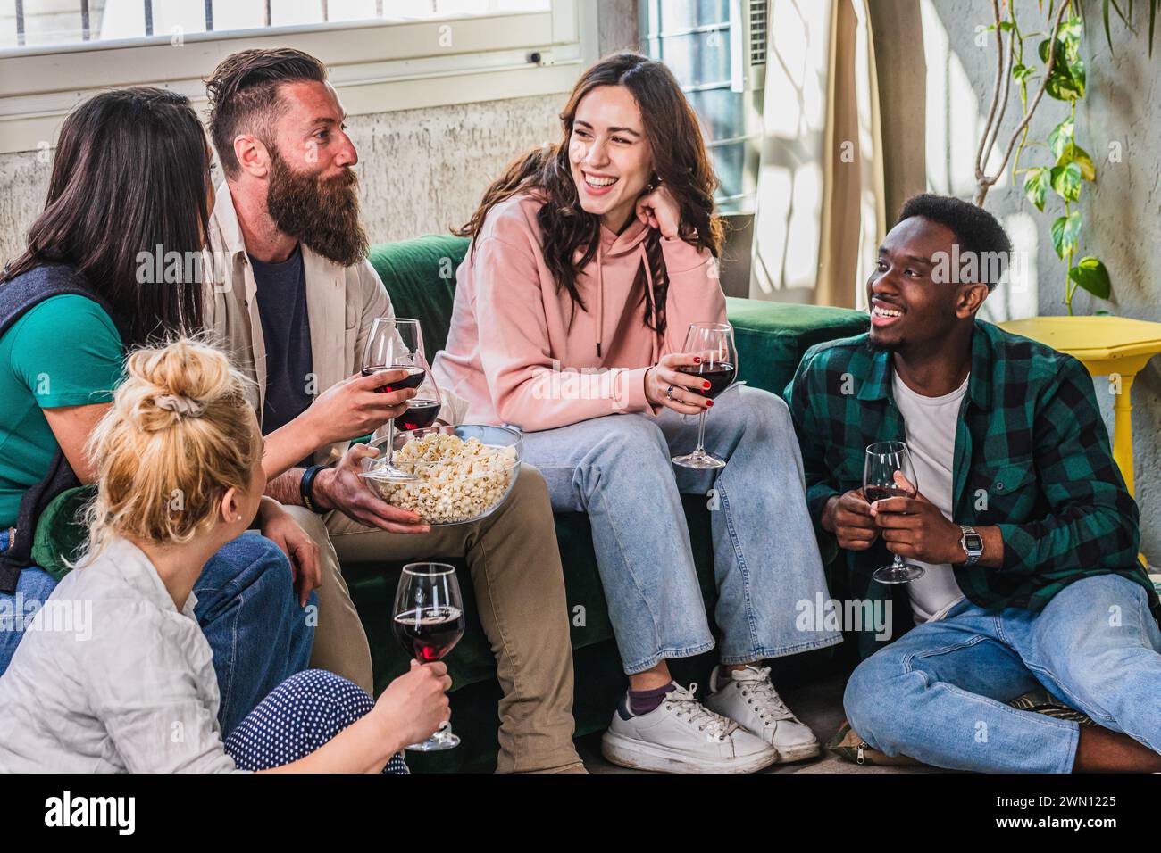 A cheerful, multicultural group of friends shares laughter over glasses ...