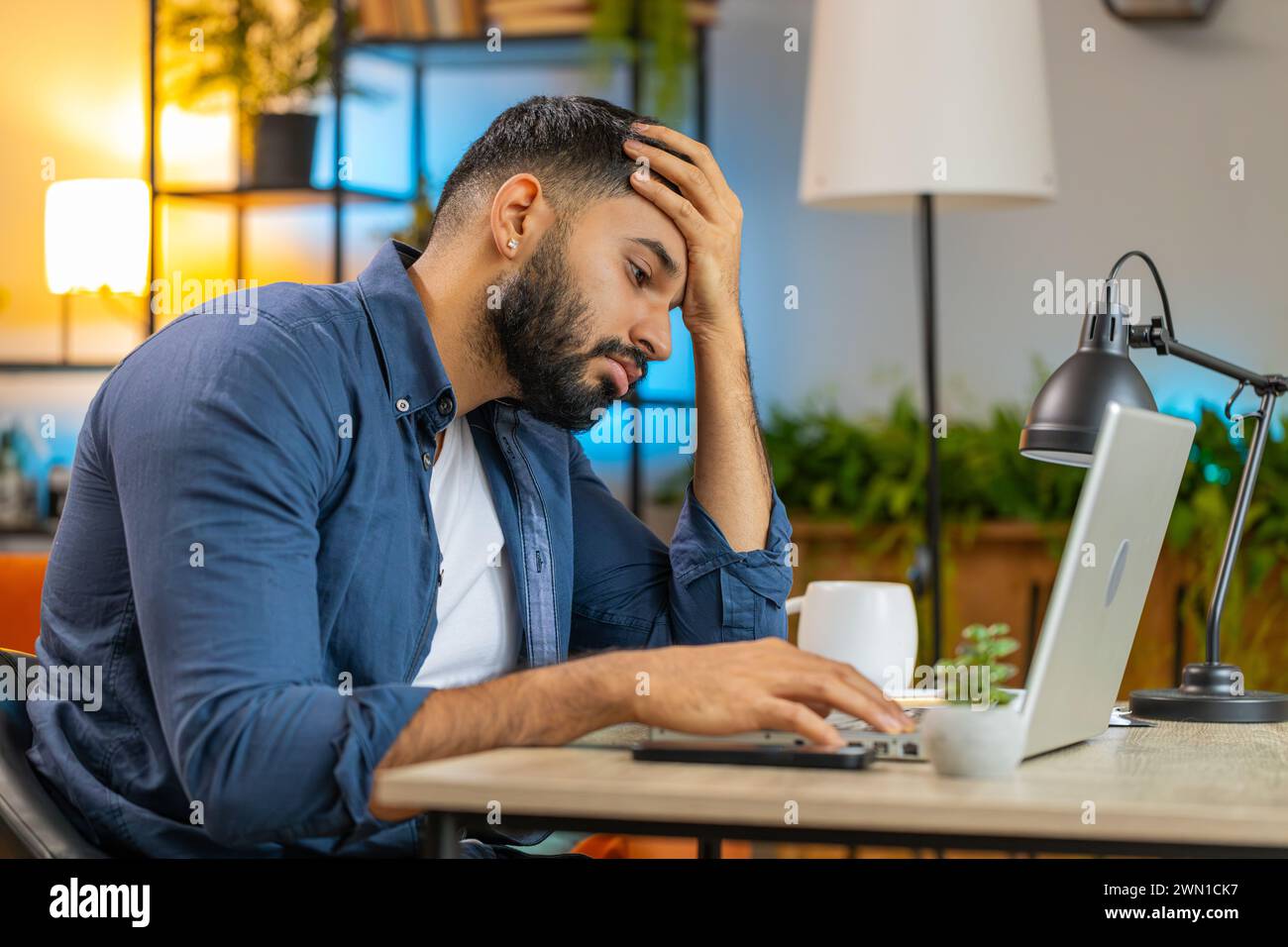 Bored sleepy young Indian bearded man working on laptop computer ...