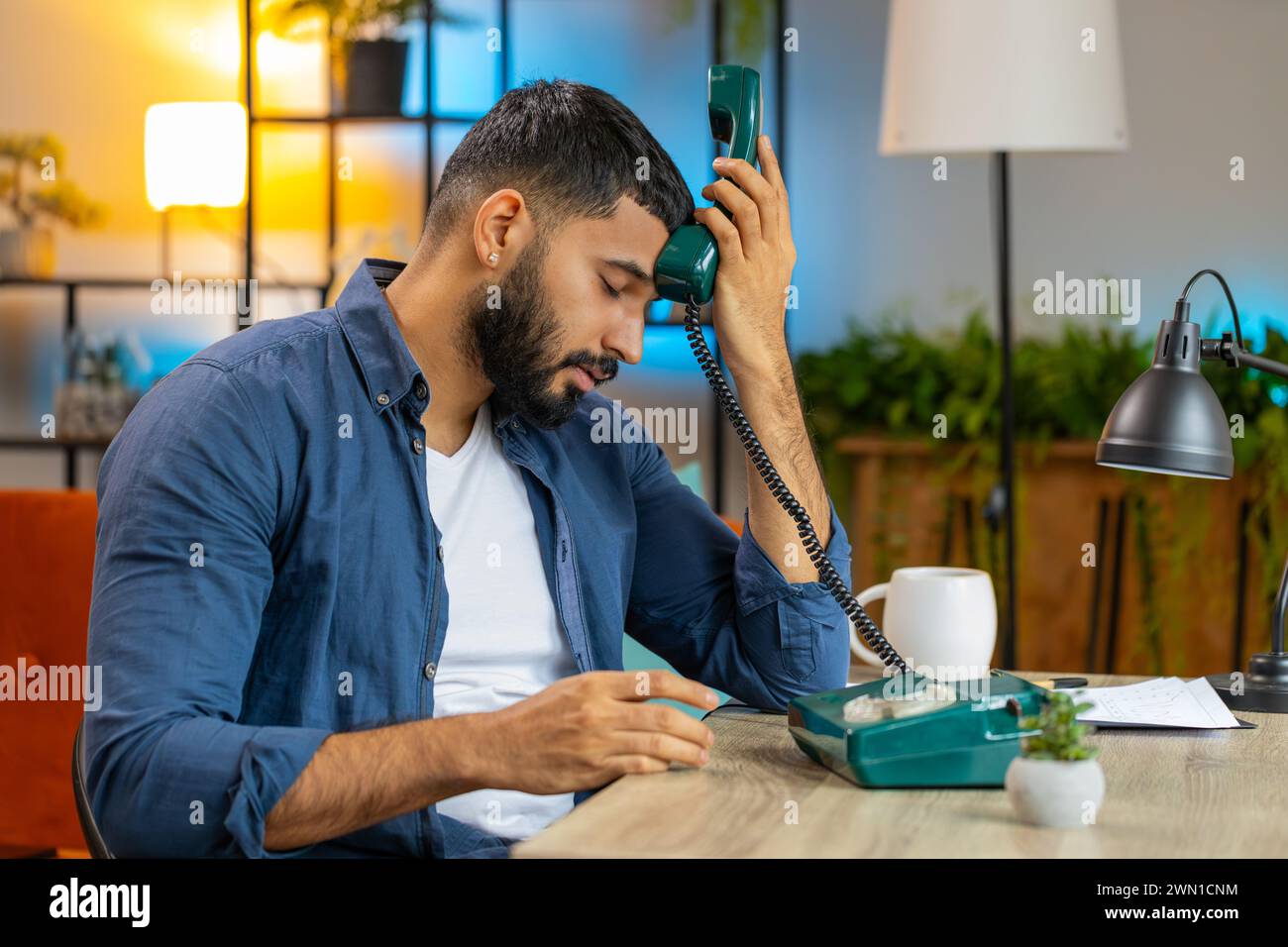 Tired bearded Indian man freelancer talking on vintage retro wired ...