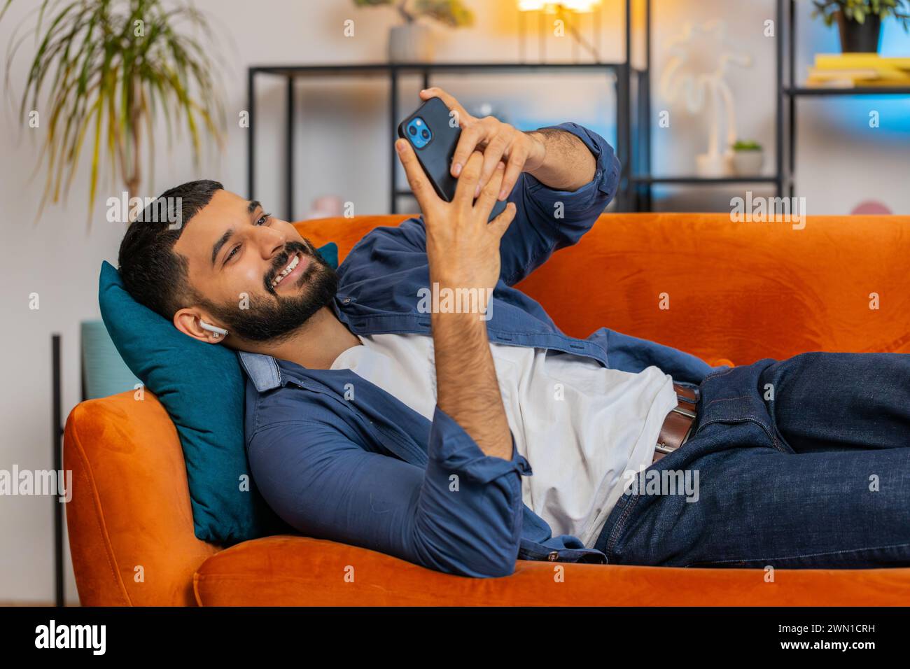 Smiling handsome Indian man taking wireless earphones out of box ...
