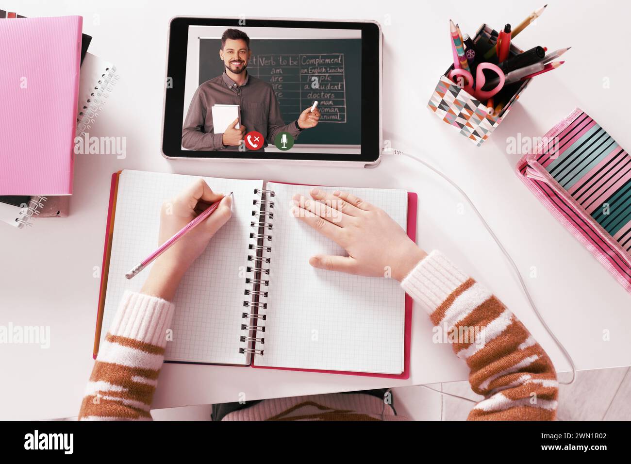 E-learning. Girl taking notes during online lesson at table indoors ...