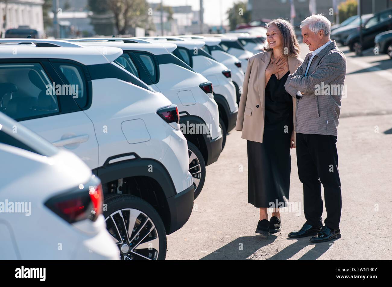 Mature Caucasian couple walks past cars outdoors, choosing a new one ...