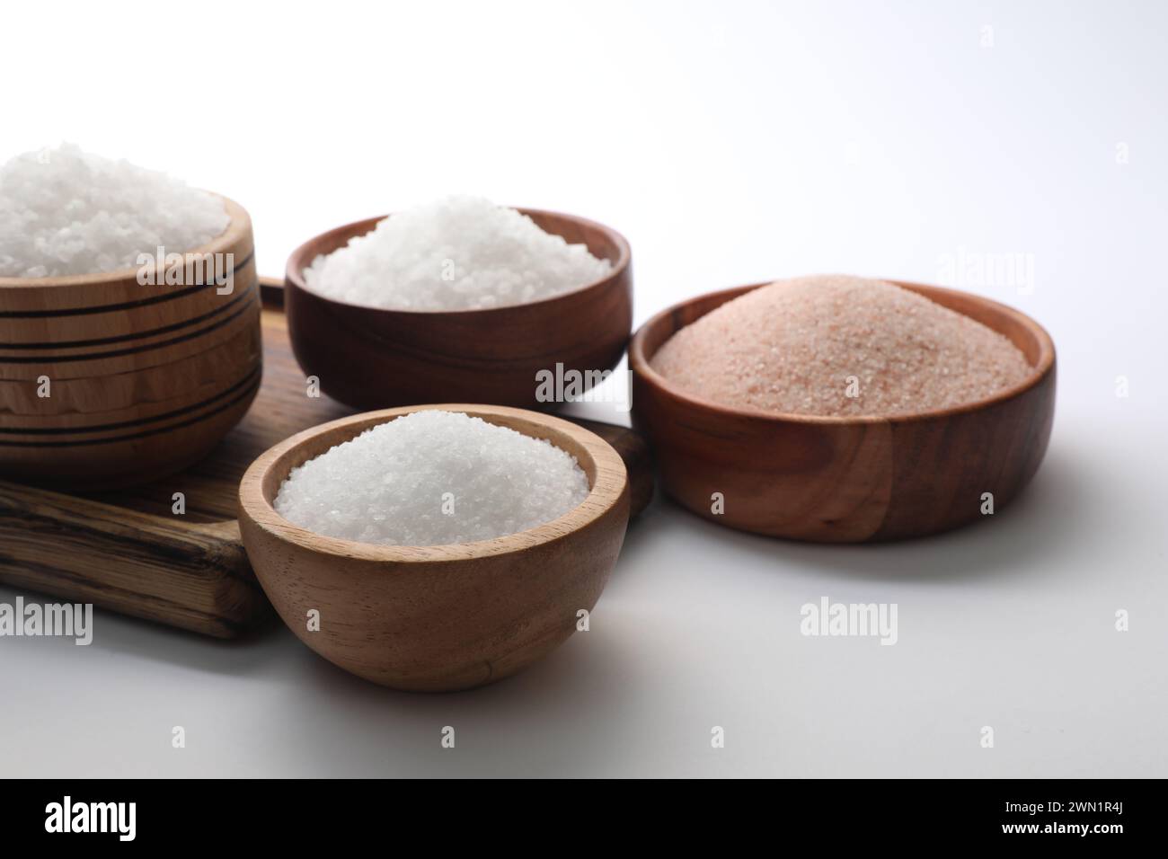 Different types of natural salt in wooden bowls on white background ...