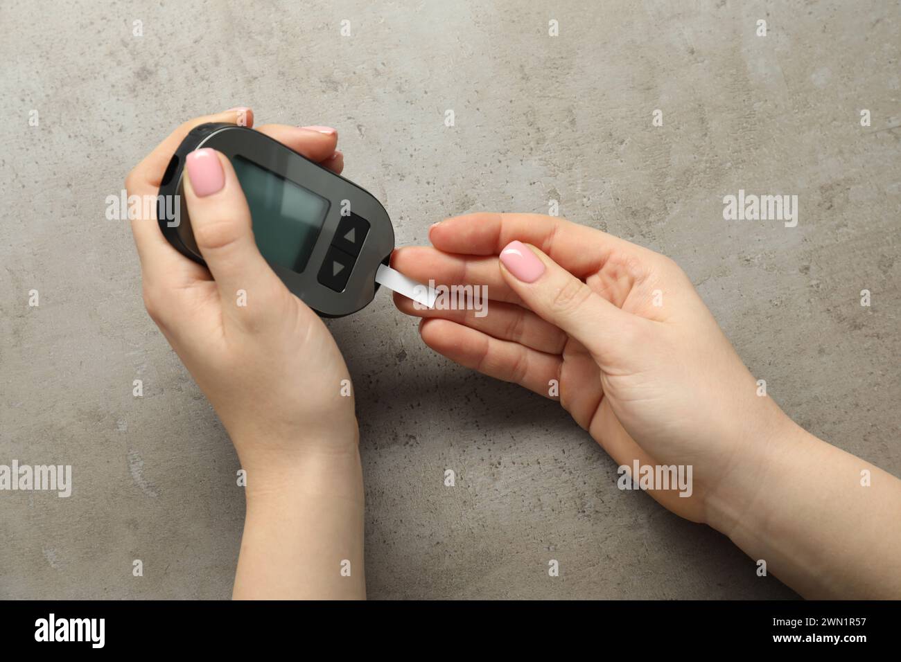 Diabetes. Woman checking blood sugar level with glucometer at gray ...