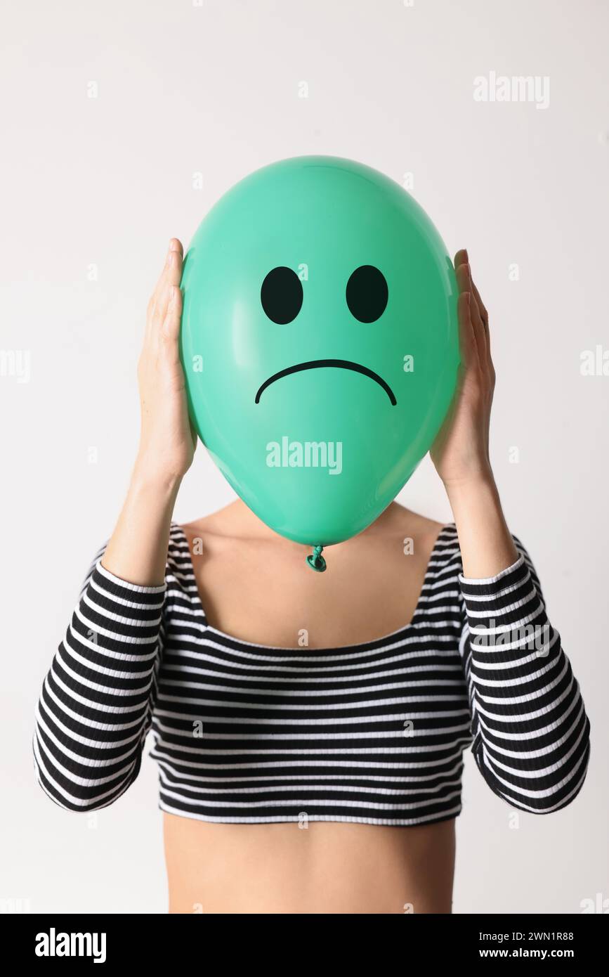 Woman hiding behind green balloon with sad face on white background ...