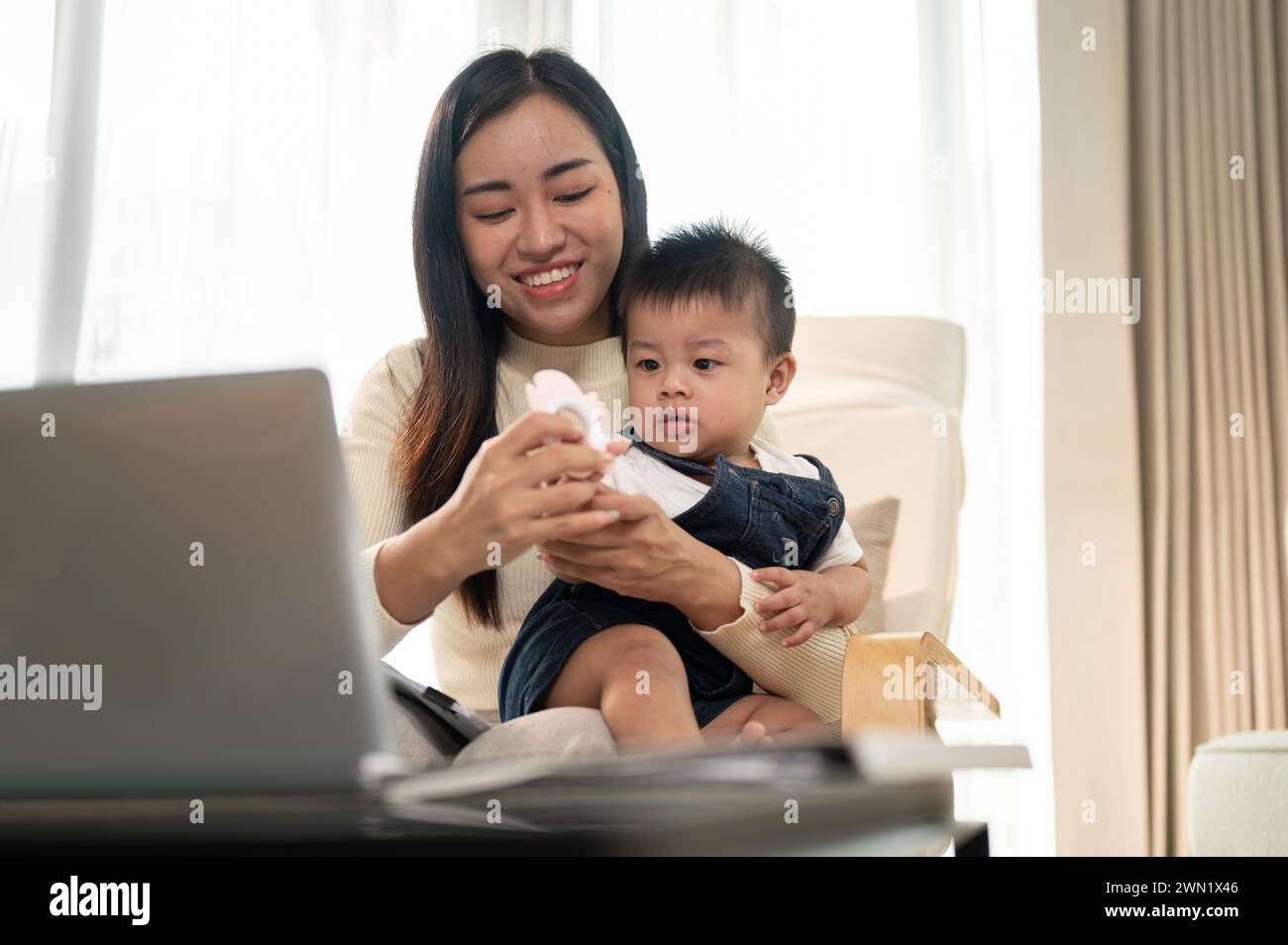 A busy Asian working woman mom is multitasking, working remotely from ...