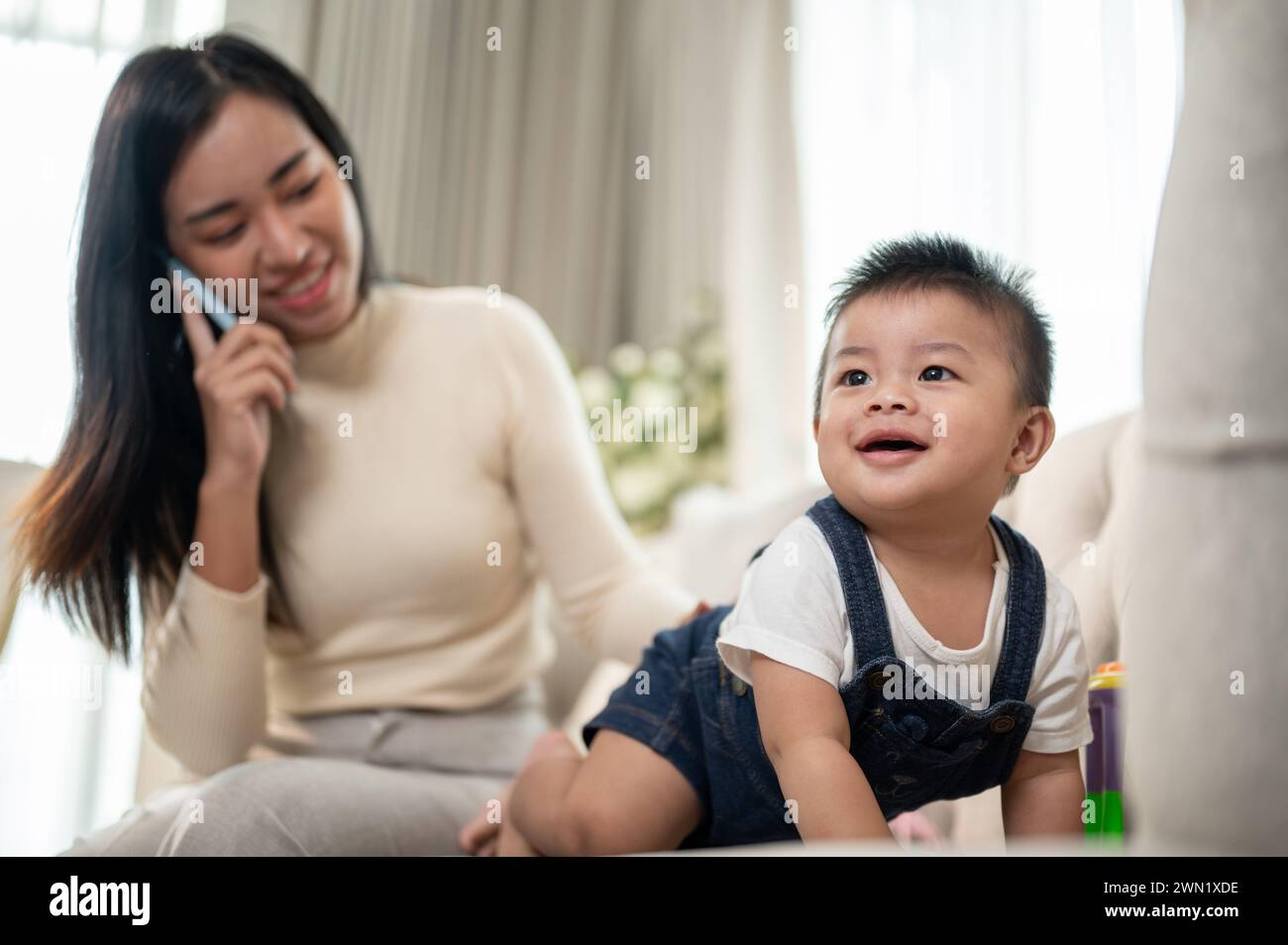 A cute, happy Asian baby boy is crawling on the floor in the living ...