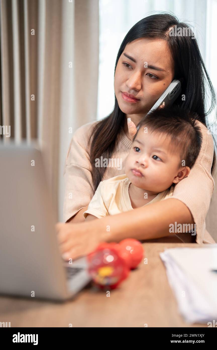 A busy Asian businesswoman mom is multitasking, talking on the phone ...