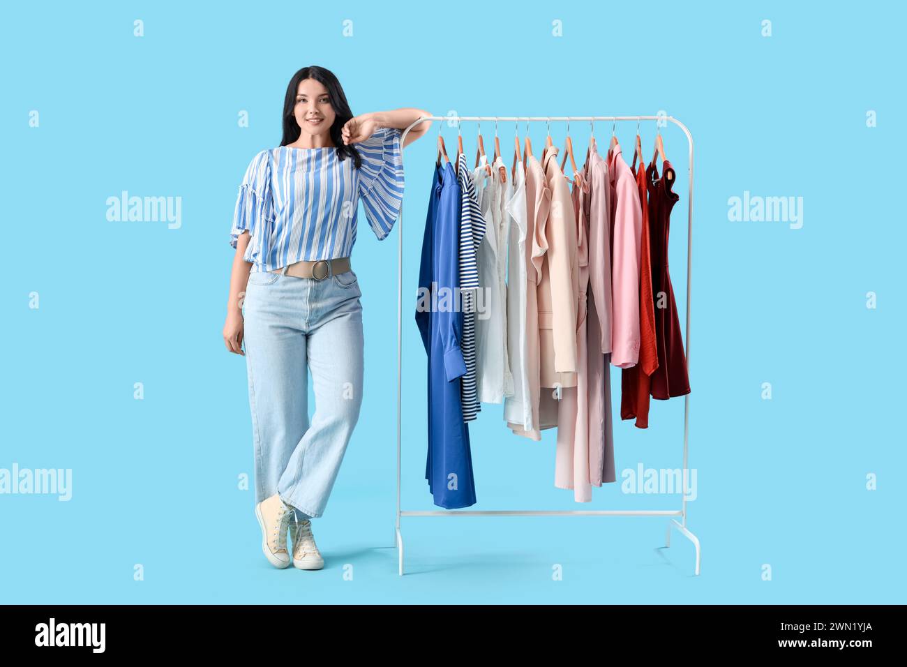 Beautiful young woman and rack with clothes on blue background Stock ...