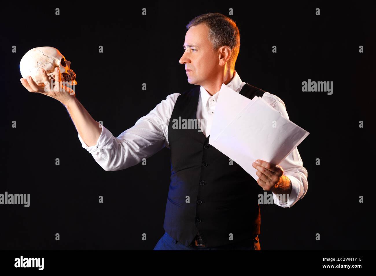 Mature actor with skull reading script on dark background Stock Photo ...
