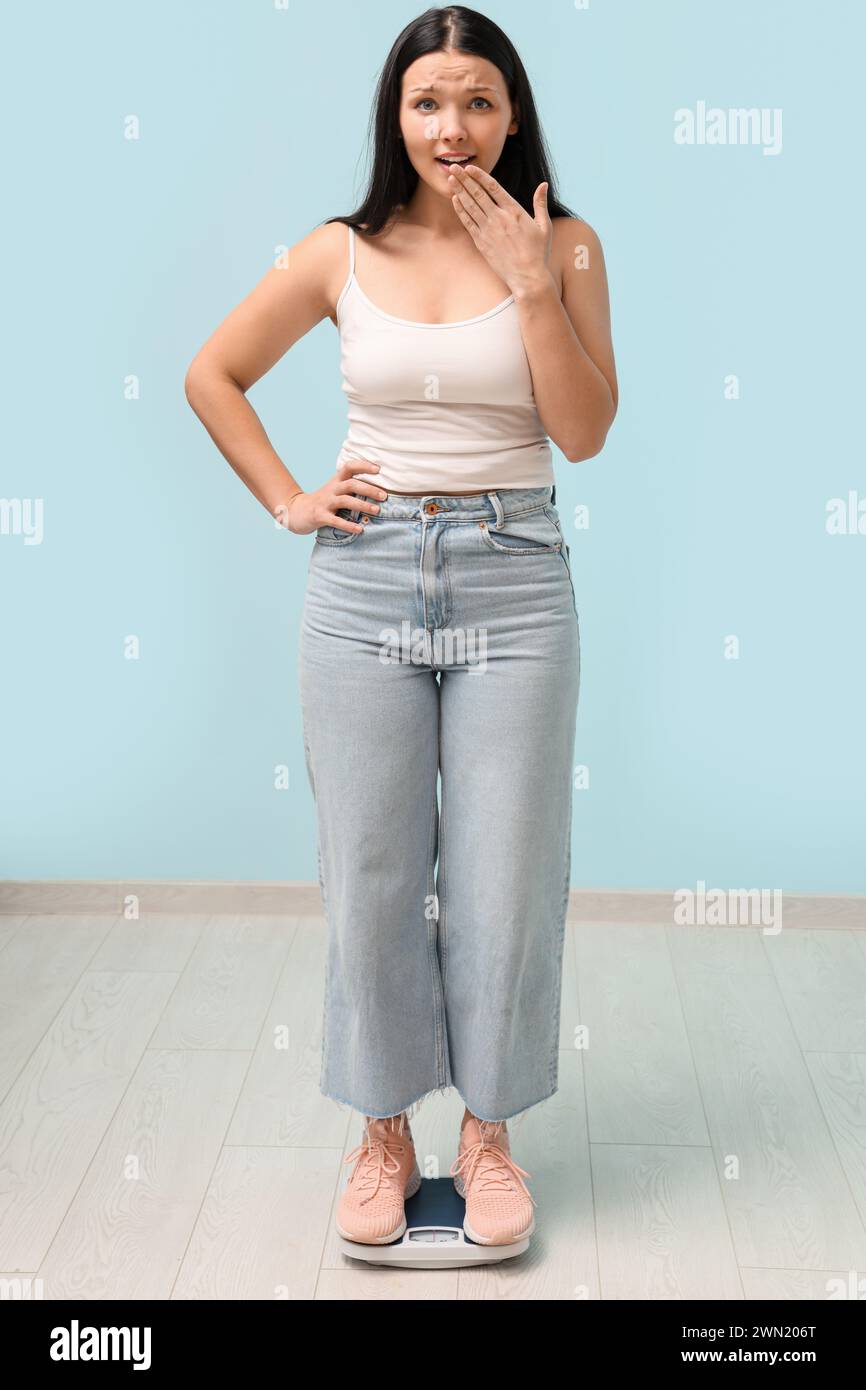 Beautiful young shocked woman with scales near blue wall. Weight loss ...