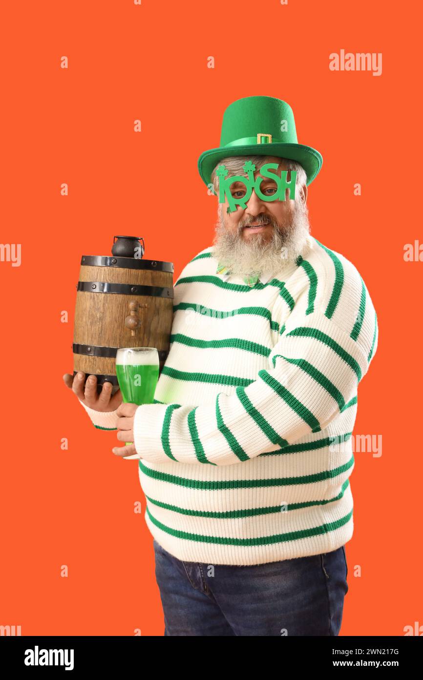 Mature man pouring beer from barrel on orange background. St. Patrick's ...