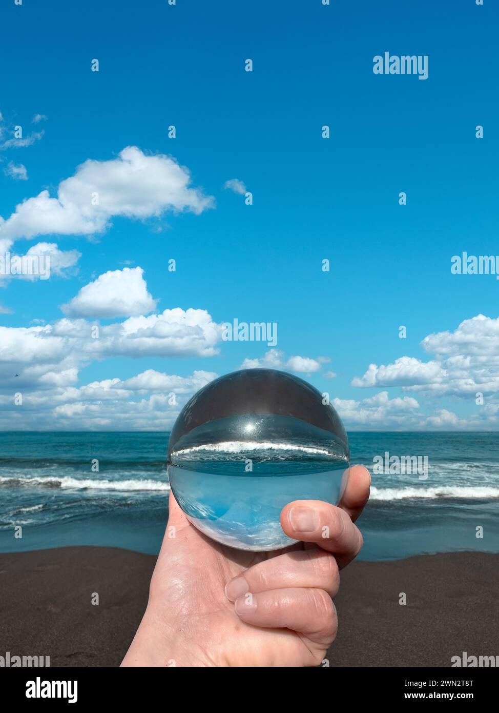 Close-up on a hand holding glass crystal ball on volcanic seaside ...