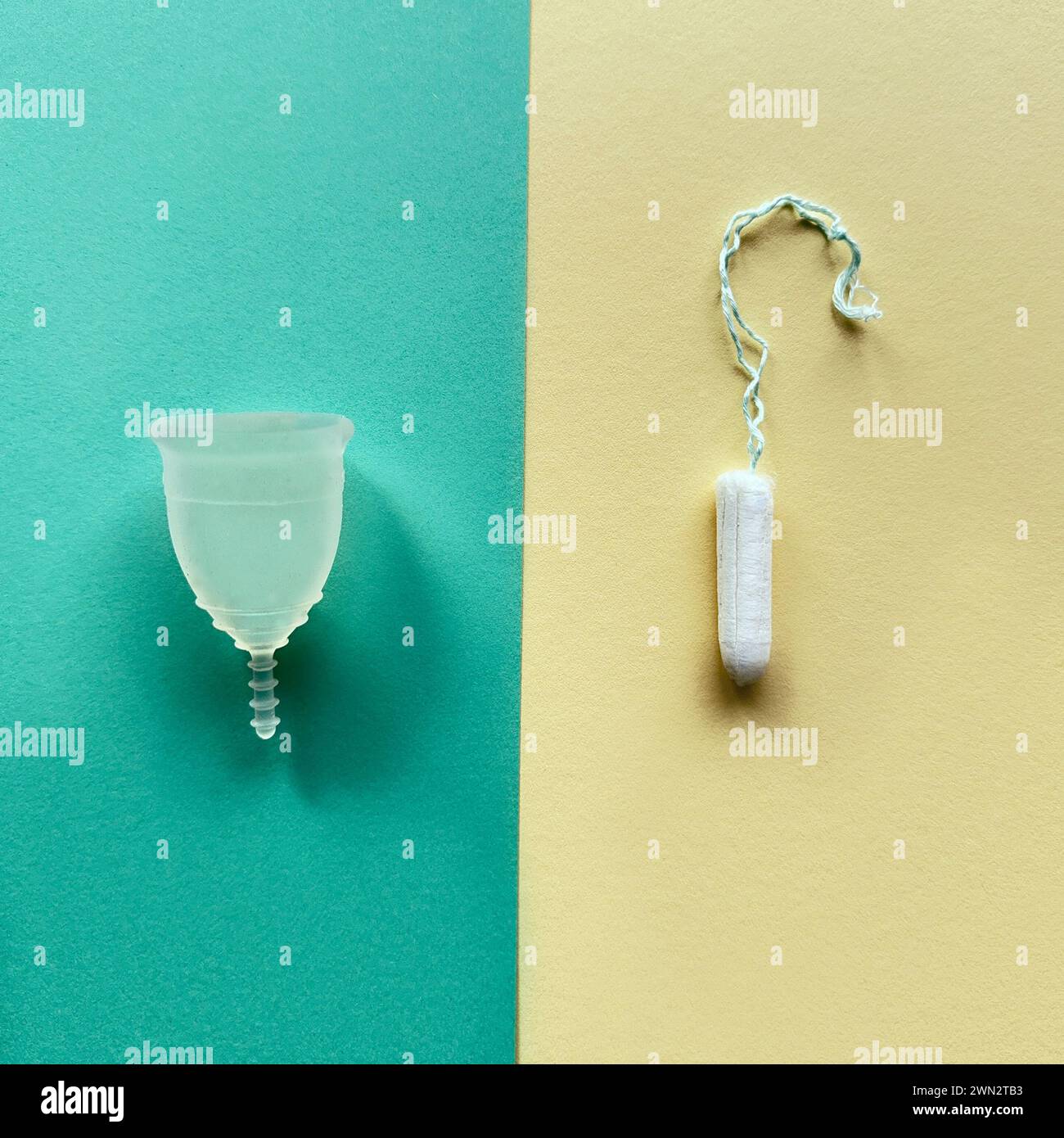 A reusable silicone menstrual cup and standard tampon on a green and ...