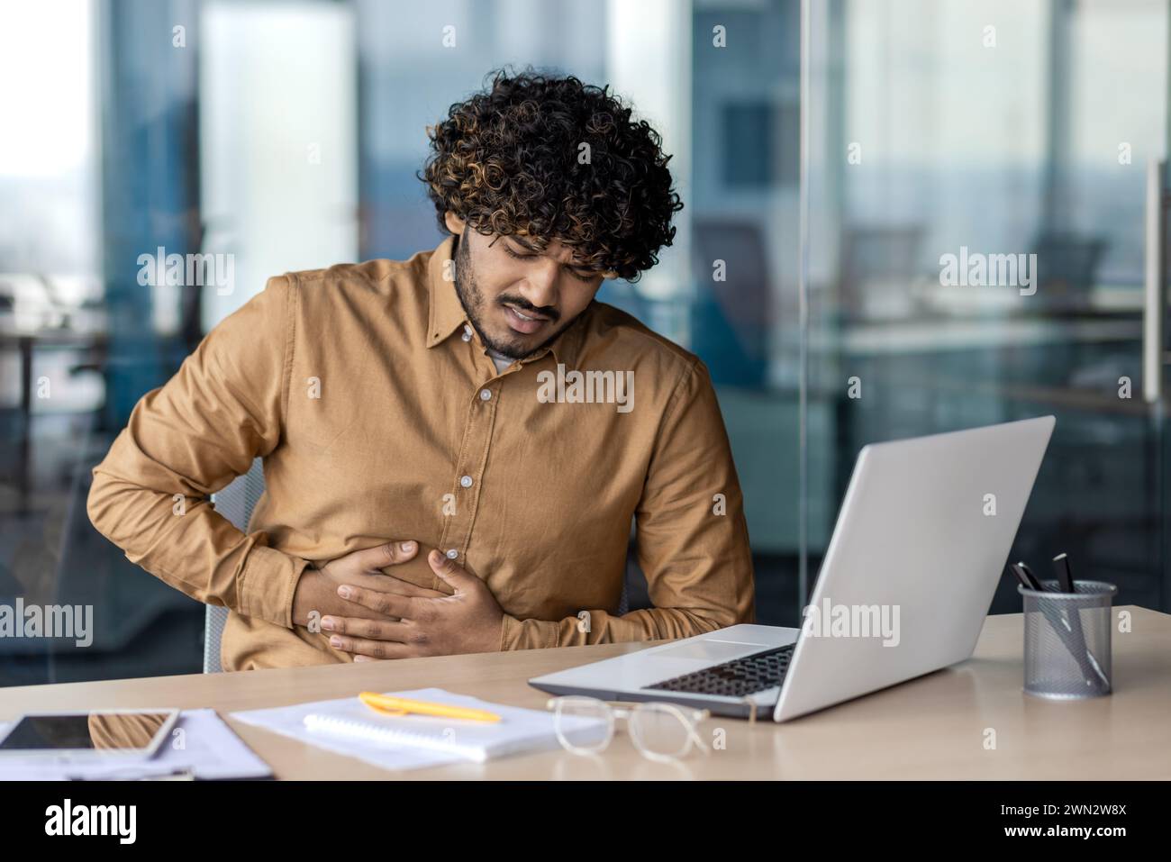 Young unhealthy man in sandy shirt touching stomach area with closed ...