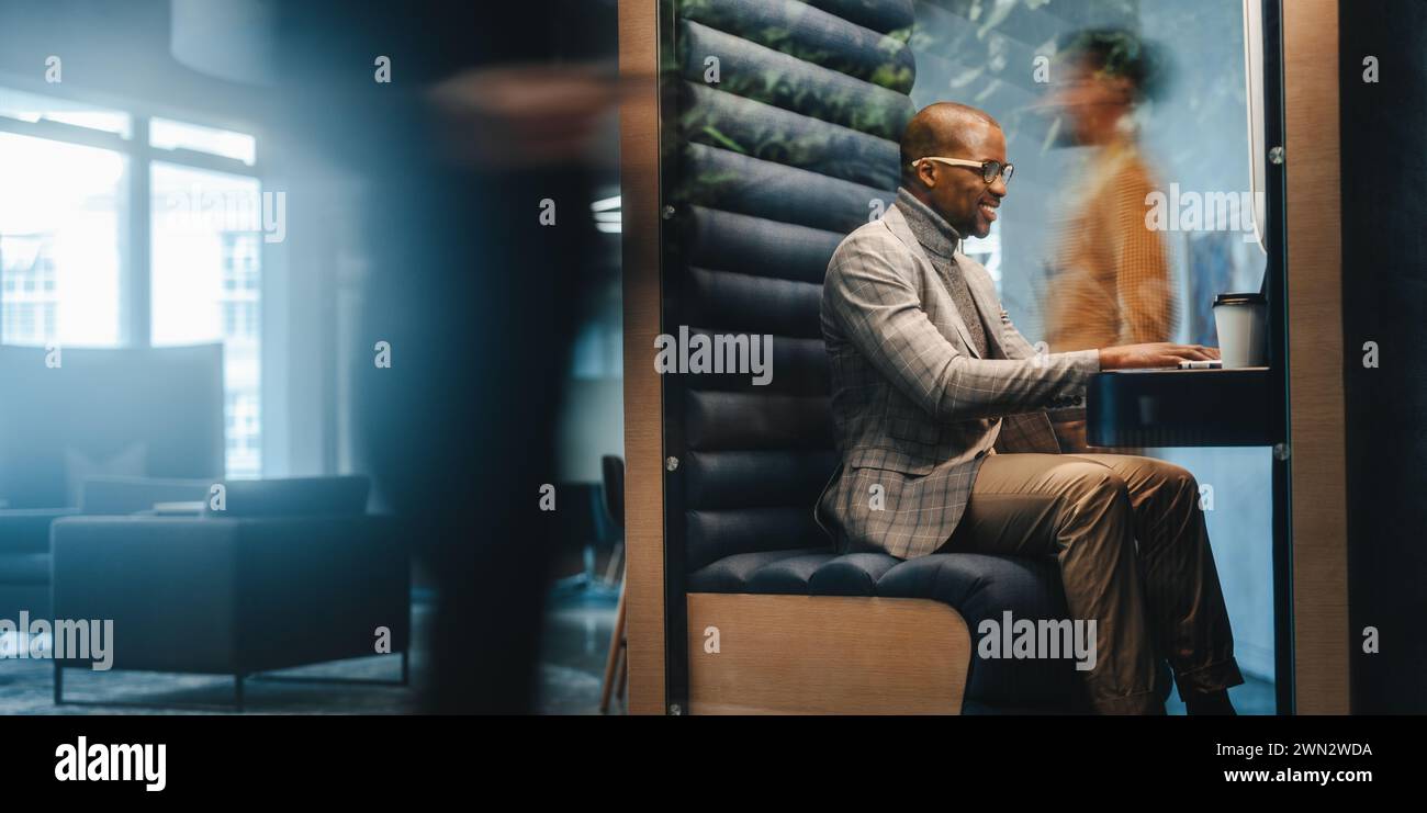 Young man sitting in a busy coworking office, working on a laptop ...