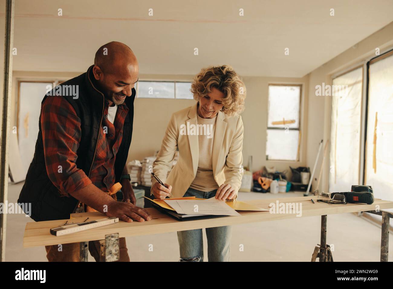 Happy homeowner and a construction worker sign an agreement for a home ...