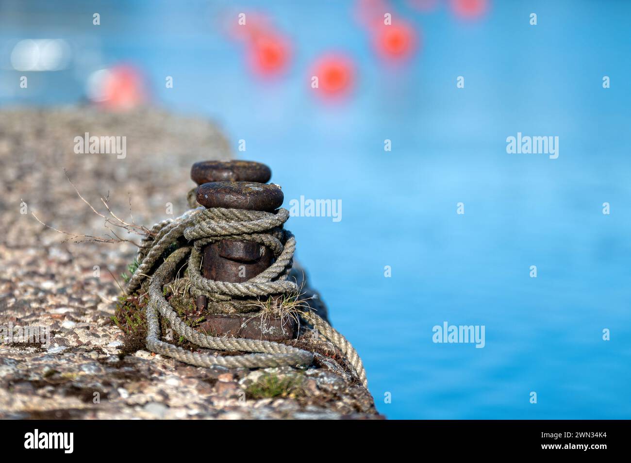 Rope tied to a mooring bollard in a harbor on the background of the sea ...