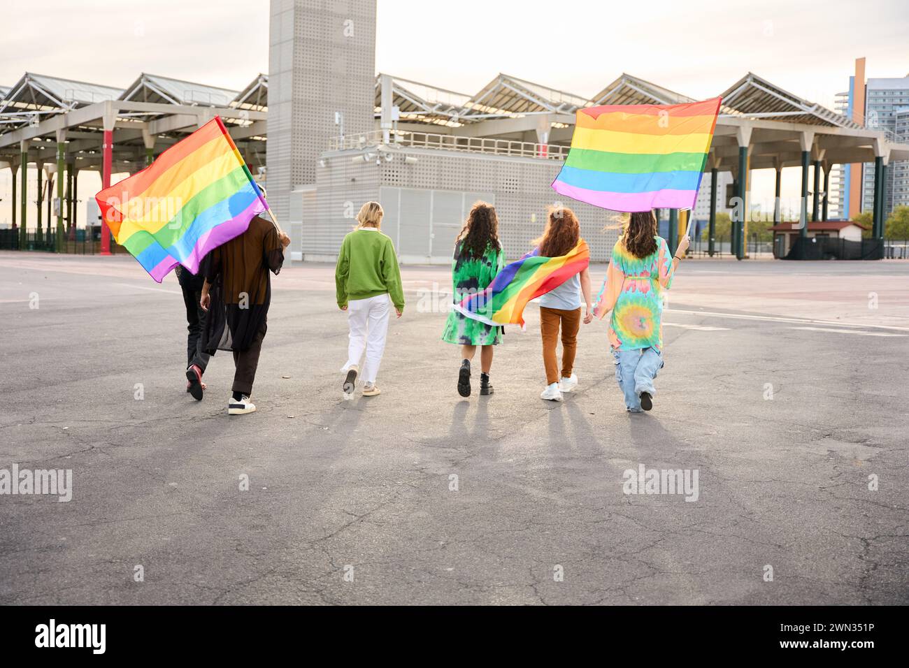 Group happy LGBT people walking down street with rainbow flags under ...