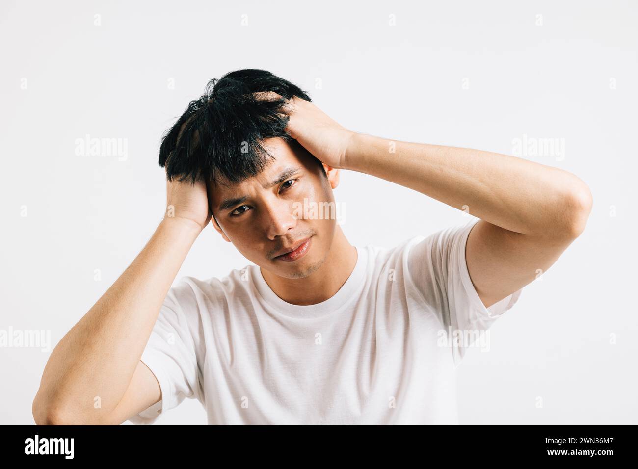 Asian man, battling stress and throbbing headache, holds head with a ...