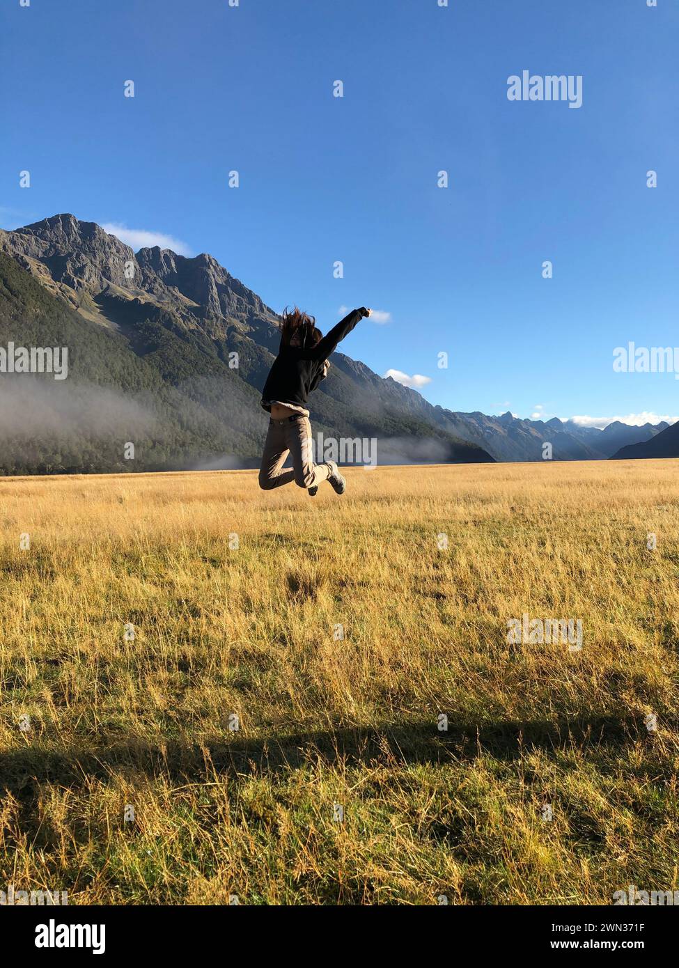 A person jumping in meadow with mountain backdrop Stock Photo - Alamy