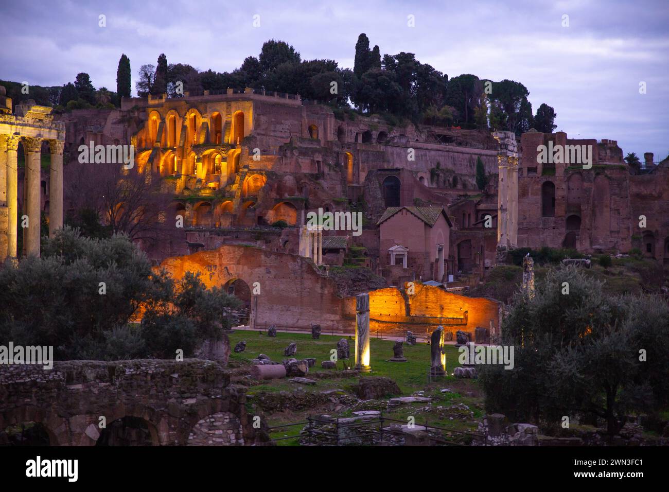 The ruins of the Roman Forum with light on at sunset in Rome, Italy ...