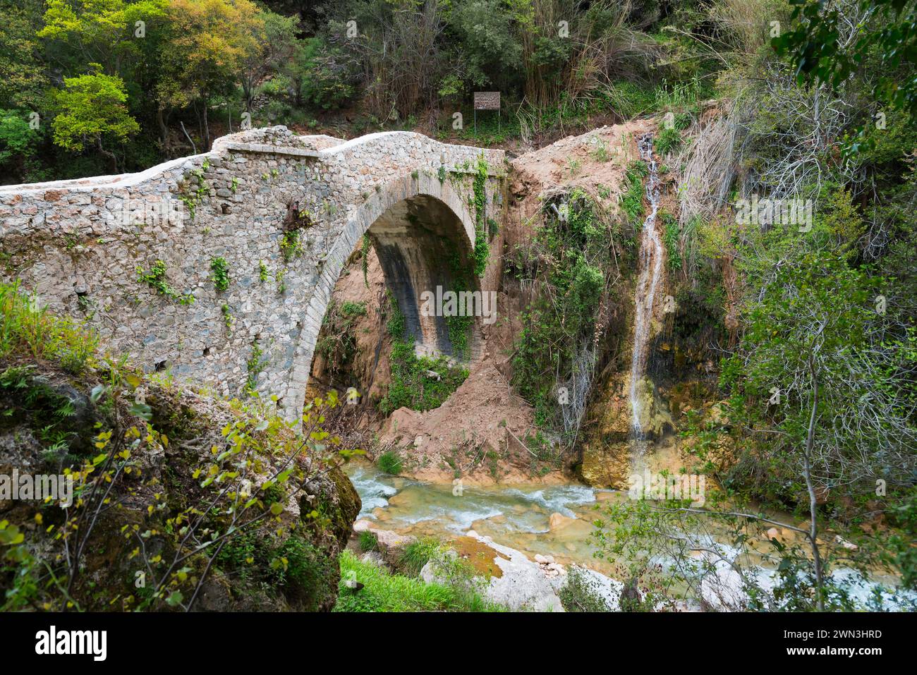 A historic arch bridge with an adjacent small waterfall in a forest ...