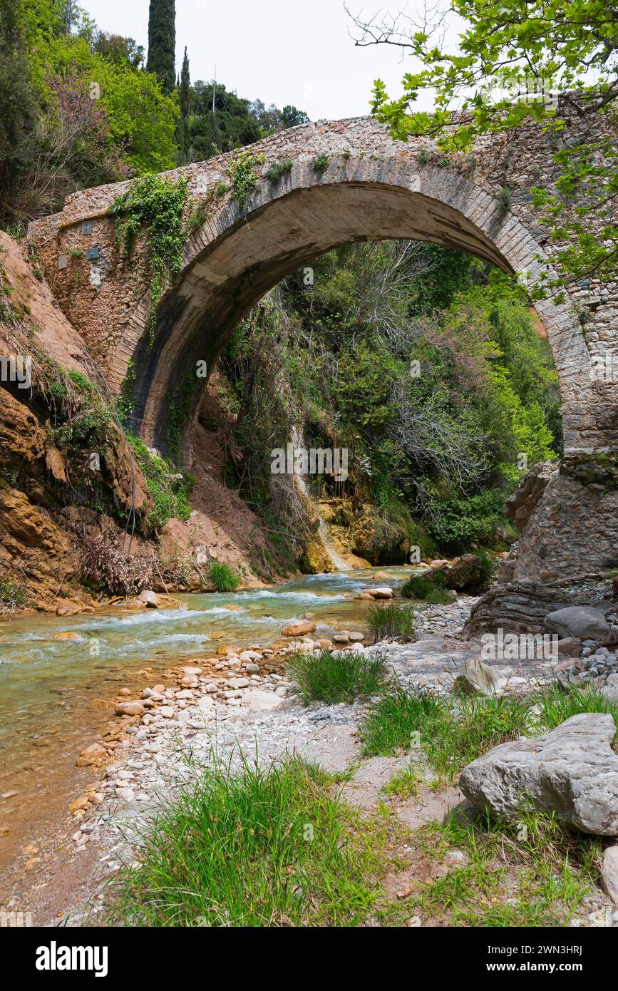 Stone arch bridge leads over a river bed with clear water in the middle ...