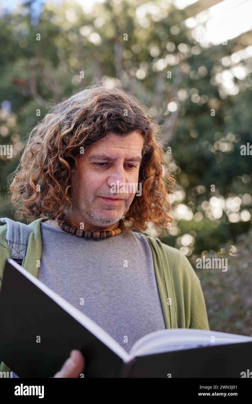 curly hair man reading a book in the park. education in middle age ...