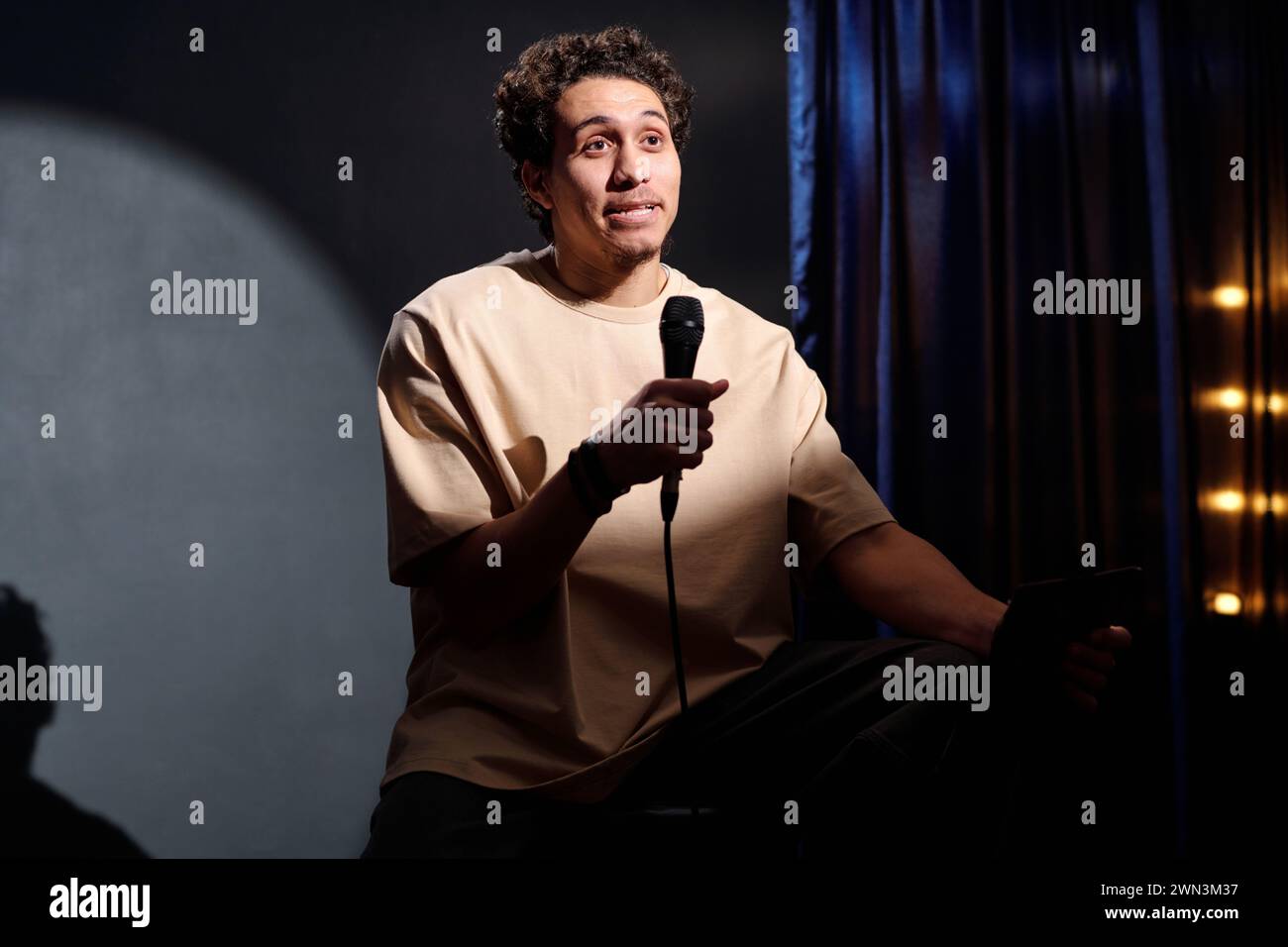 Young male stand up comedian performing his monologue while sitting on ...