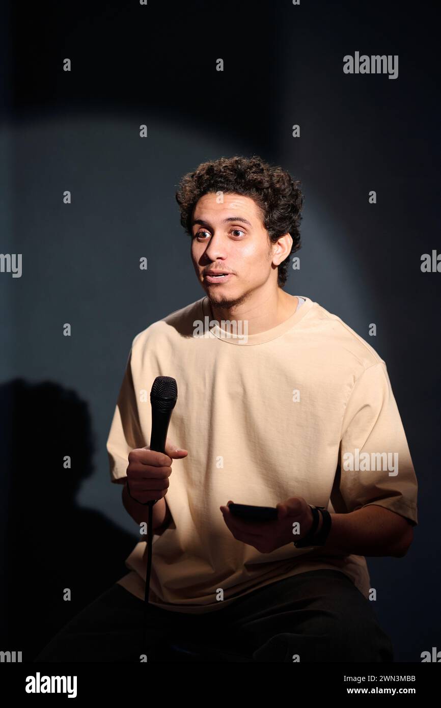 Young comedian, actor or showman with microphone and smartphone sitting ...